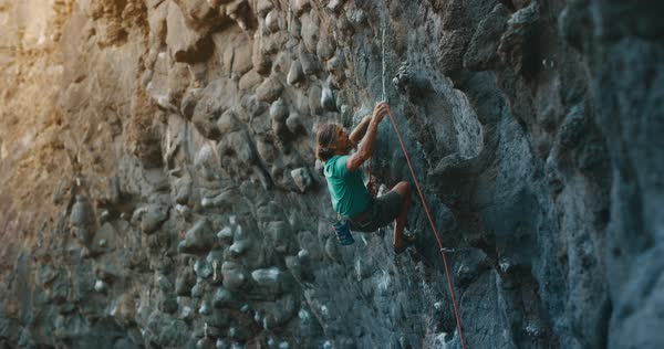Strong male rock climber lead climbing on a sport route, clipping into ...