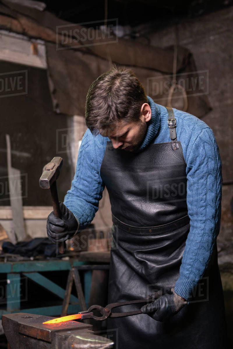 Blacksmith forging hot metal with hammer at anvil in blacksmith shop ...