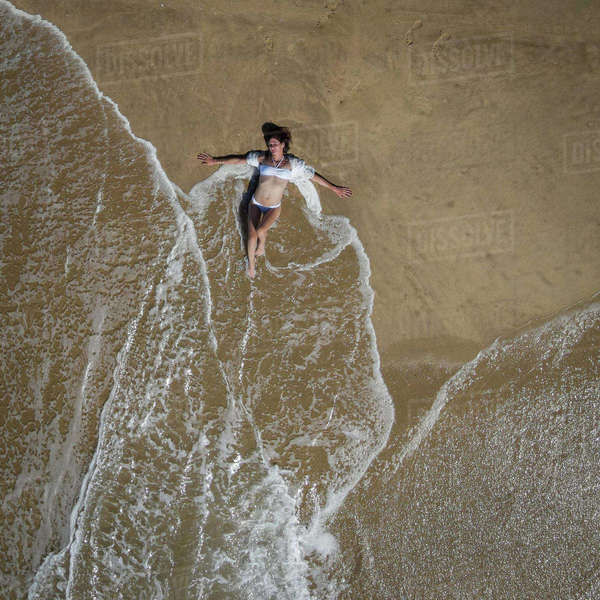 Aerial view of a woman in a bikini lying in ocean surf on a beach ...