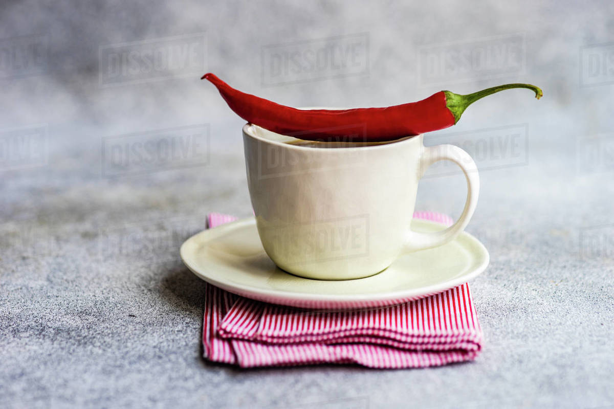 Close-Up of a cup of coffee with a red chilli pepper on a folded napkin ...