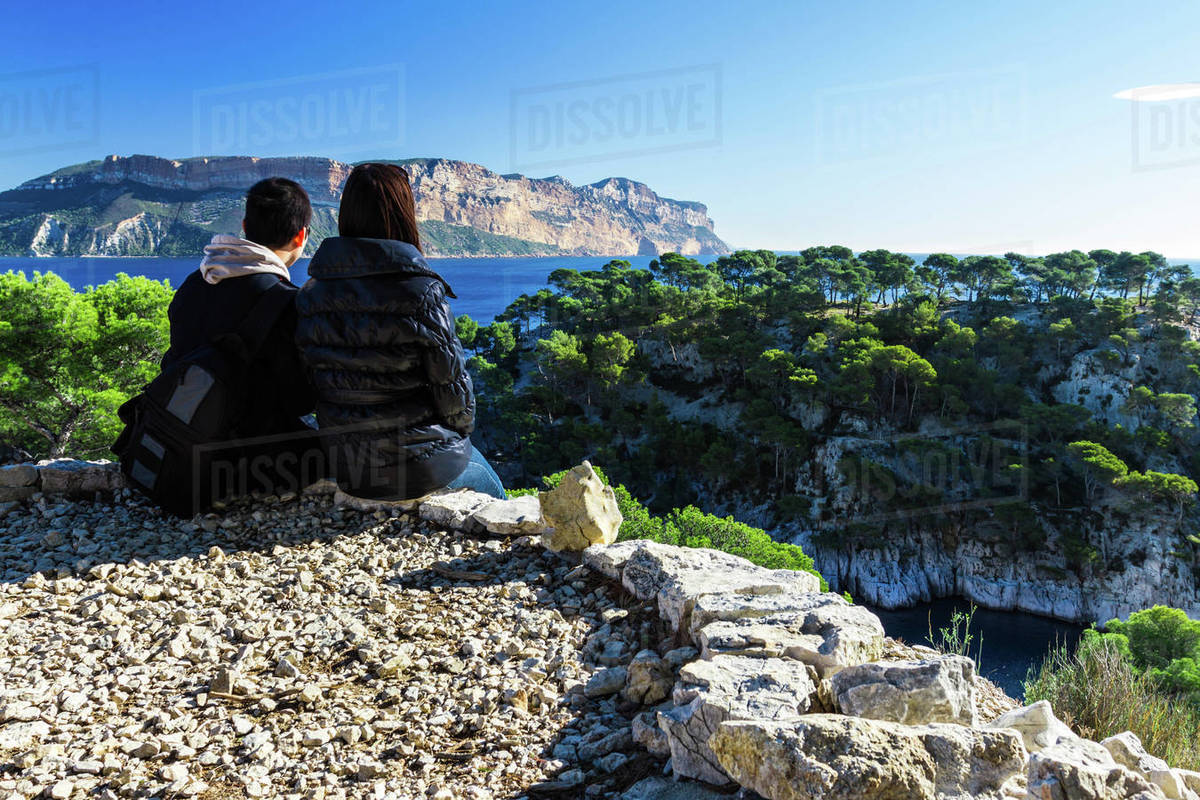 Rear view of a couple sitting on rocks, Les Calanques, Cassis, Bouches ...