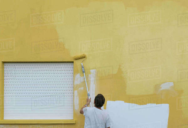 Rear view of a man painting a house yellow with a paint roller, Spain ...