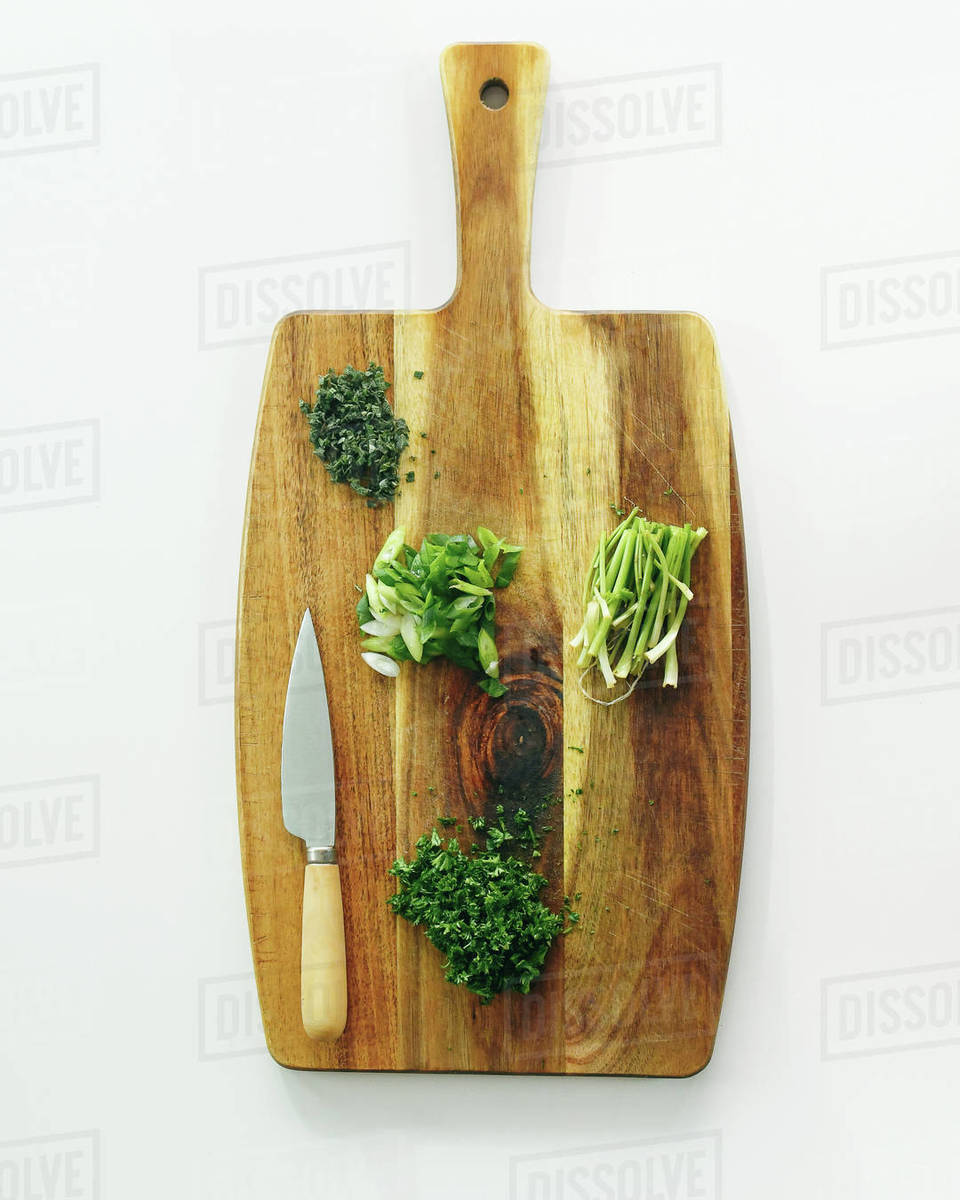 Overhead view of chopped herbs on a wooden chopping board with a knife ...