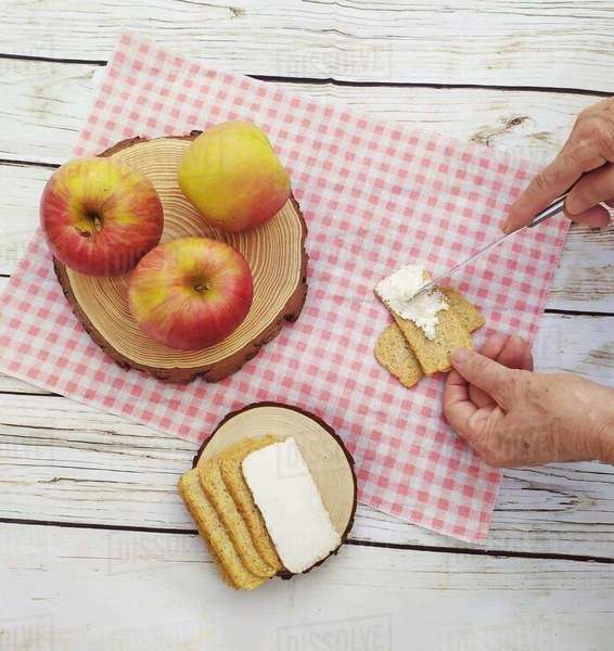 Overhead view of a person spreading cream cheese on a cracker with ...