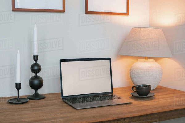 Open laptop with a blank screen, candlesticks and a lamp on a table ...