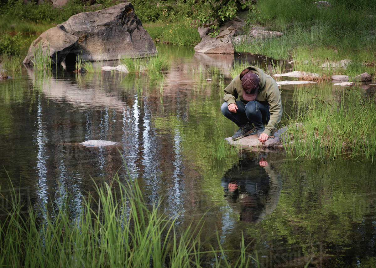 Woman crouching on a rock looking down into water, Lake Lemolo, Oregon ...