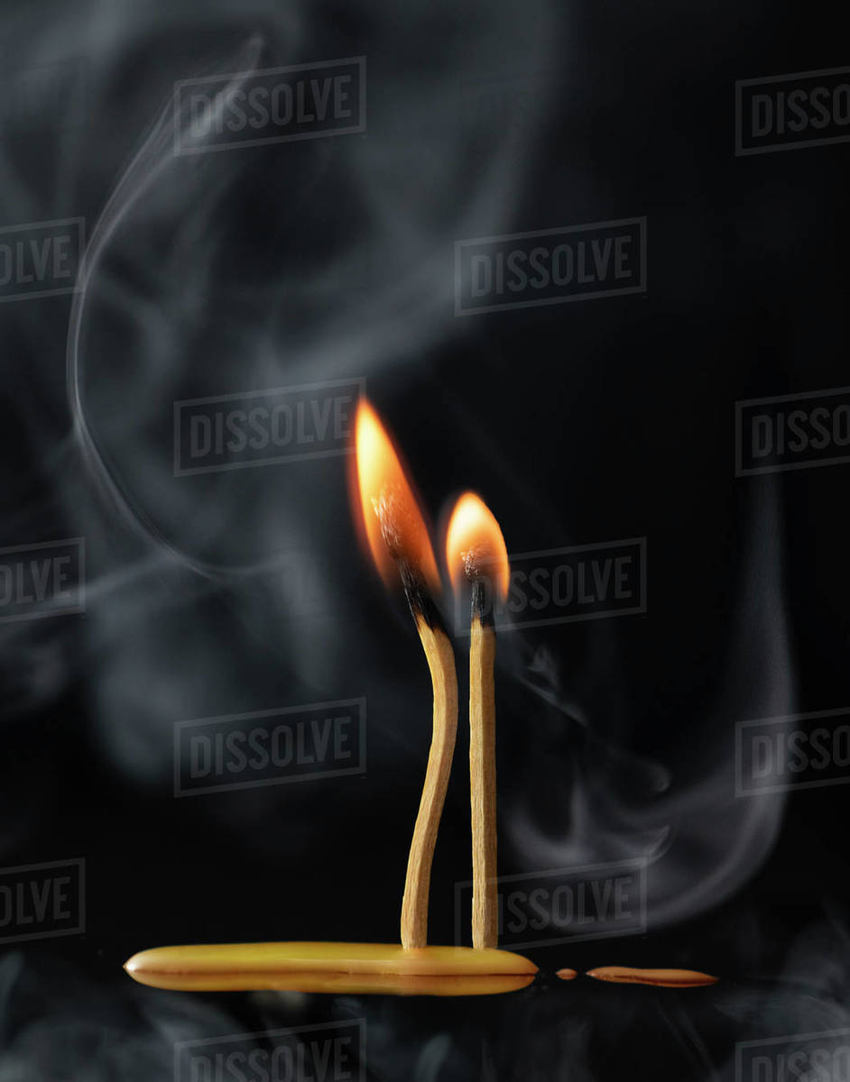 Close-up of two burning matchsticks and smoke against a black ...