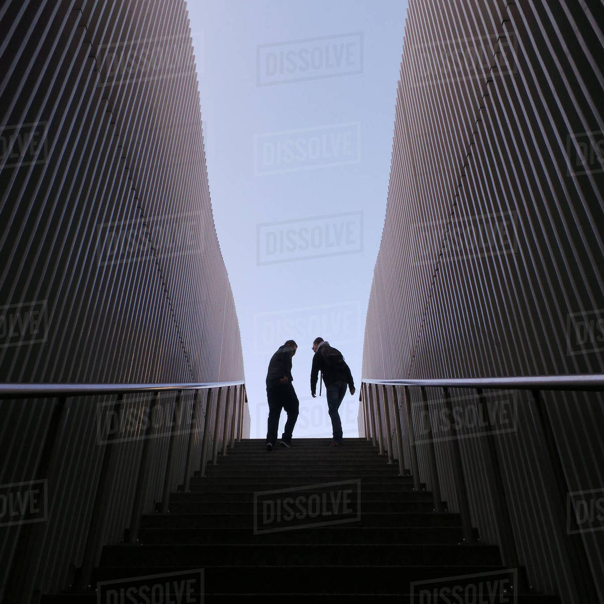 Symmetrical image of two silhouette people on top of stairs, walls on ...