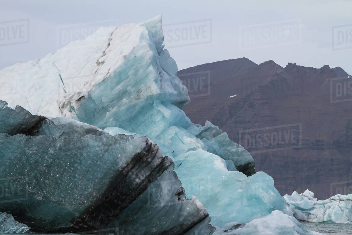 Close-up of a black striped iceberg with mountains in the background ...