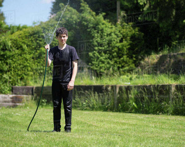 Boy holding a hose pipe, cooling down by spraying water over his head ...