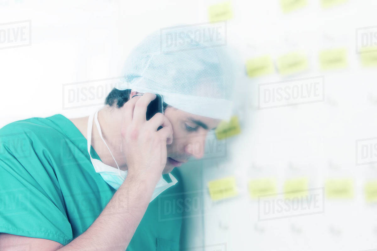 Surgeon standing in front of schedule board talking on mobile phone ...