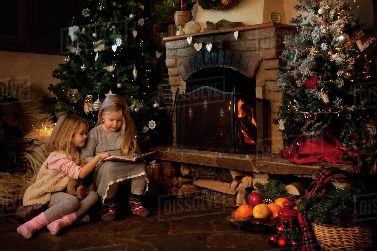 Two girls sitting in a living room on Christmas Eve reading a book ...