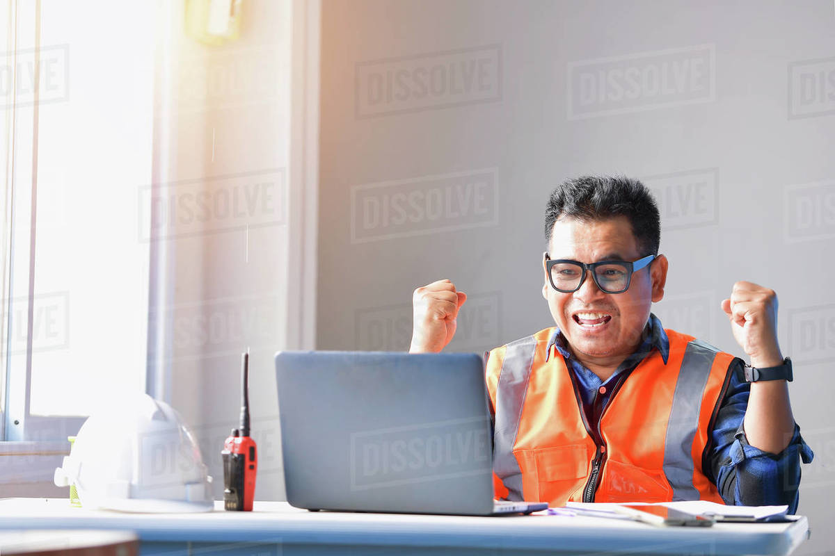 Smiling engineer sitting at his desk celebrating with his hands in the ...