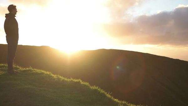 Young man staring into the sunset while seing mountains and ocean ...