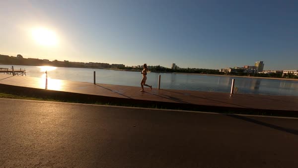 FPV drone tracking shot of sporty female runner jogging along wooden ...