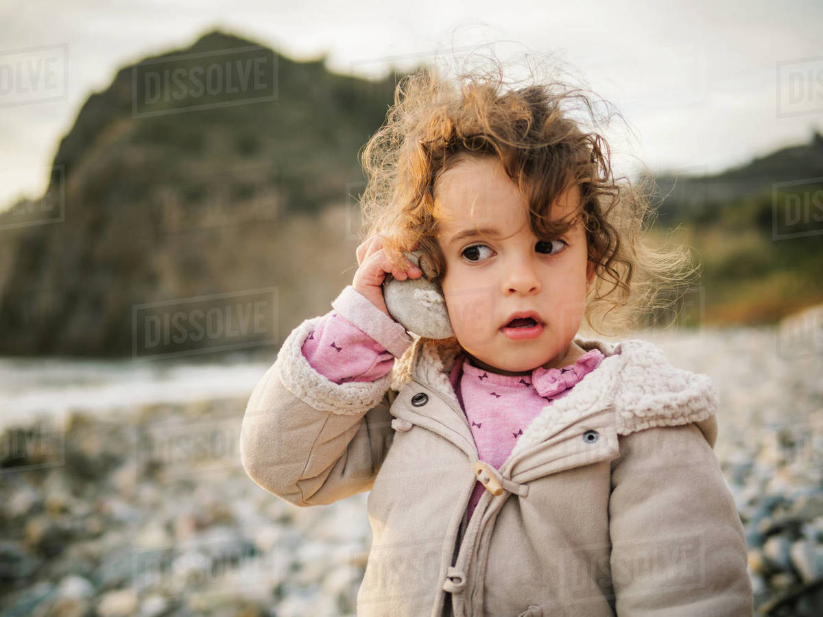 Portrait of cute female kid listening to conch with rapt attention ...