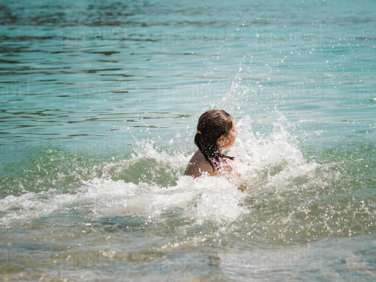 Back view of anonymous joyful cute girl playing in water of sea on ...