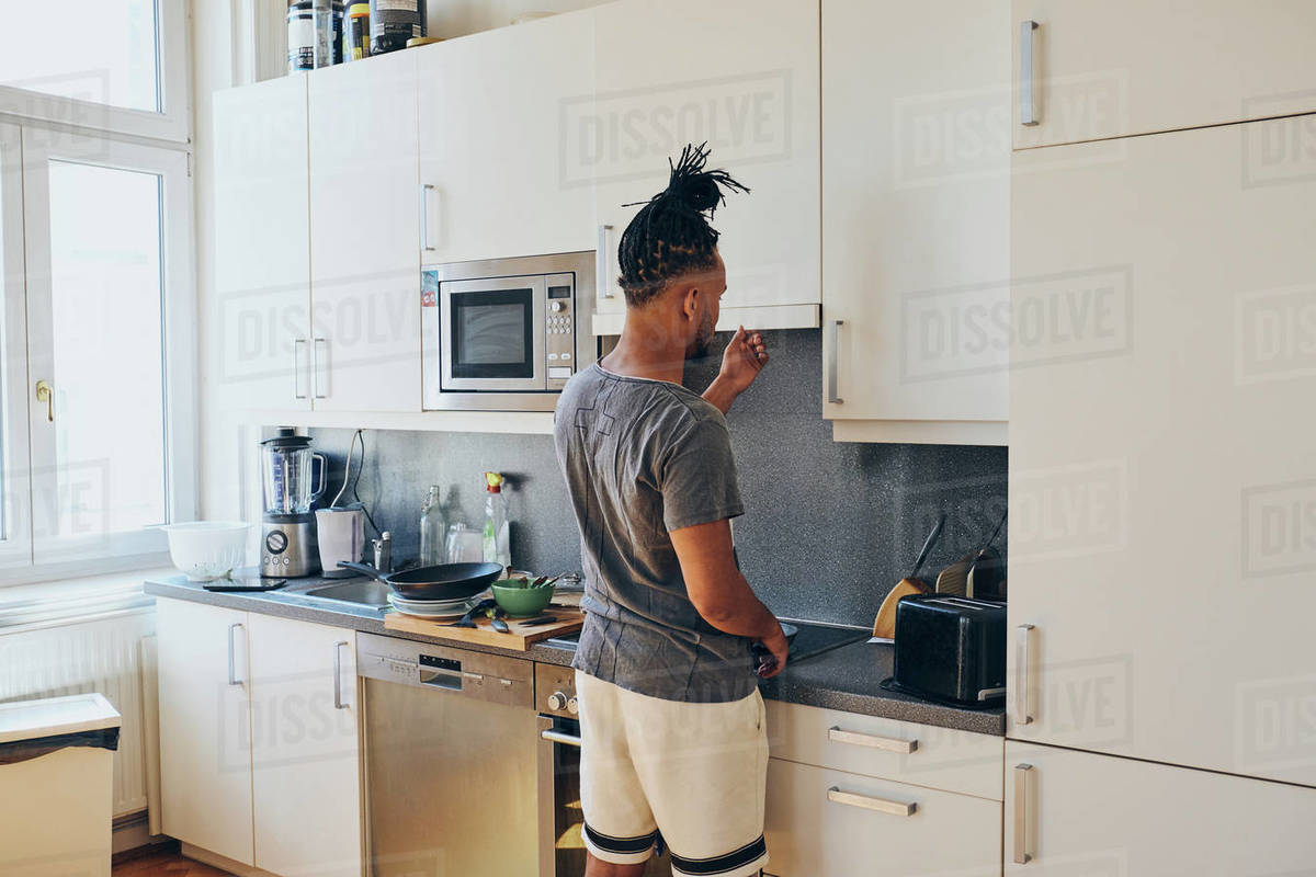 Side view of African American braided man standing in kitchen with ...