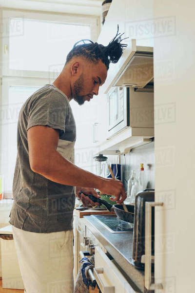 Side view of African American braided man standing in kitchen with ...