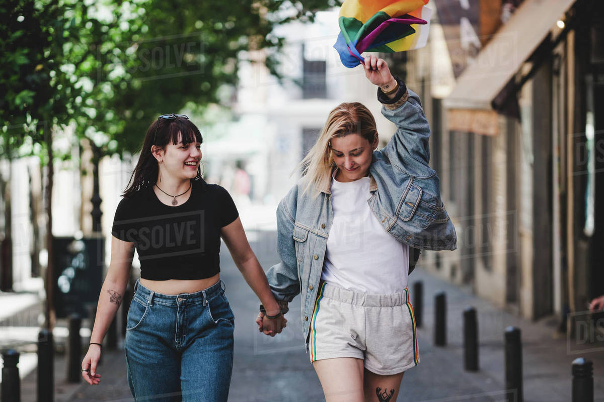 Cheerful Lesbians Holding Hands And Waving Lgbt Flag While Walking On