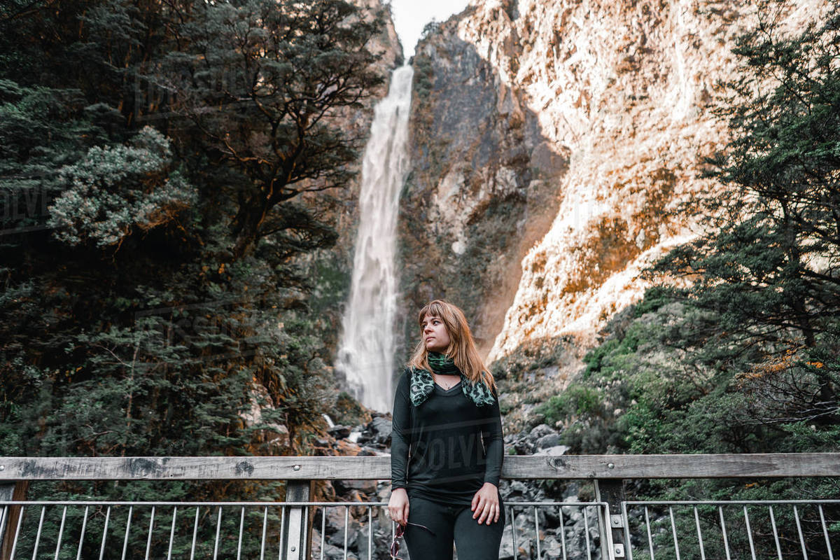 From below attractive woman leaning on fence around waterfall near Lake ...