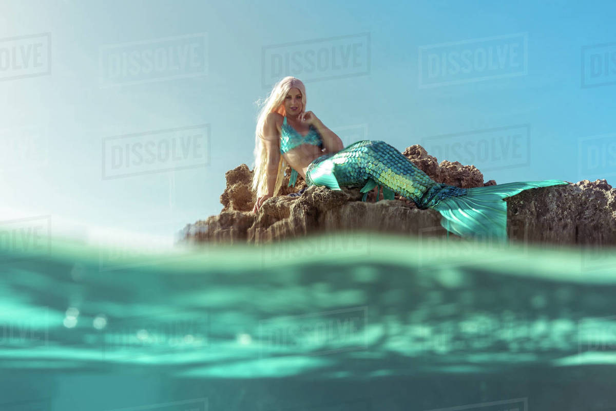 Beautiful young mermaid with blue fishtail relaxing on cliff on sunny ...