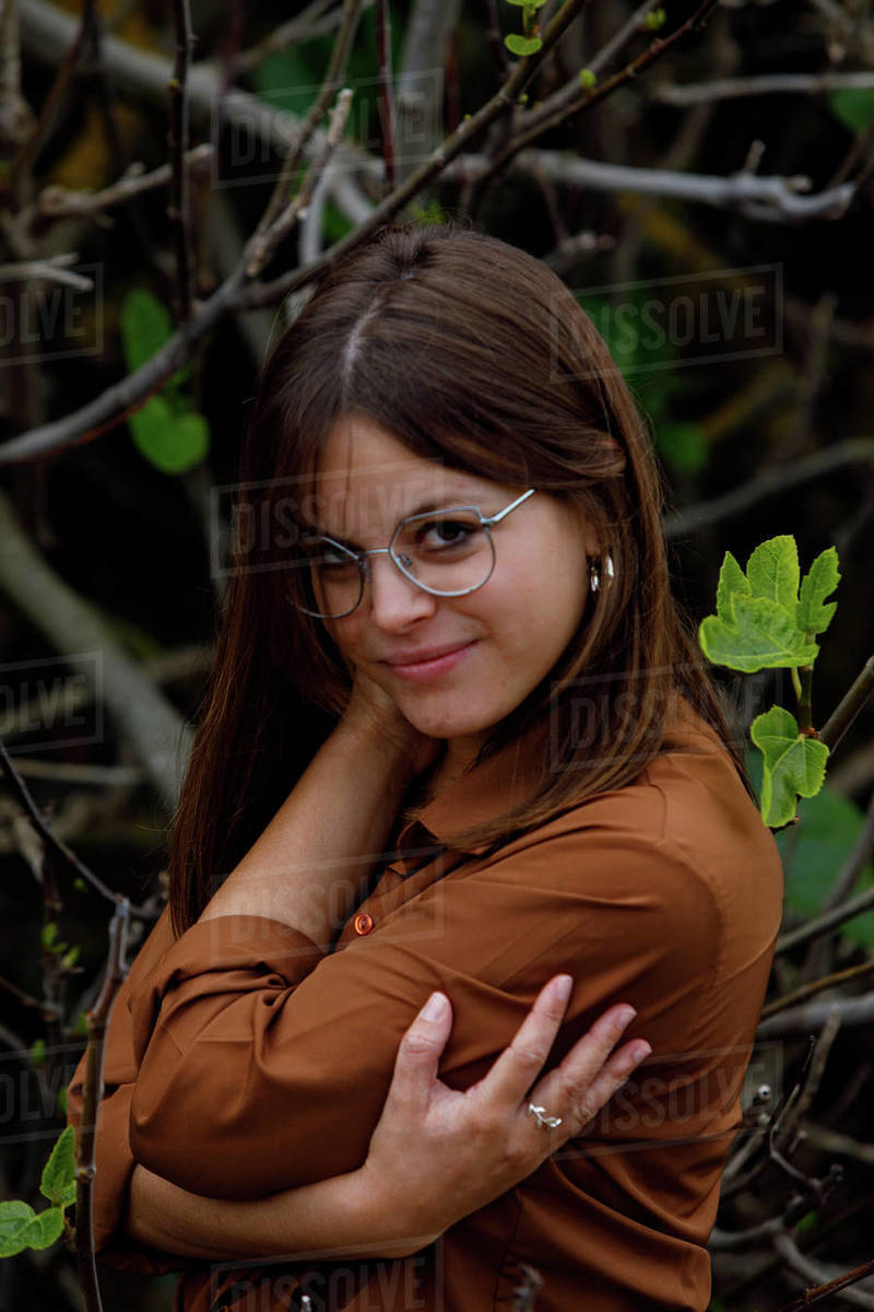 Side view of beautiful woman standing in front of bushes looking at ...