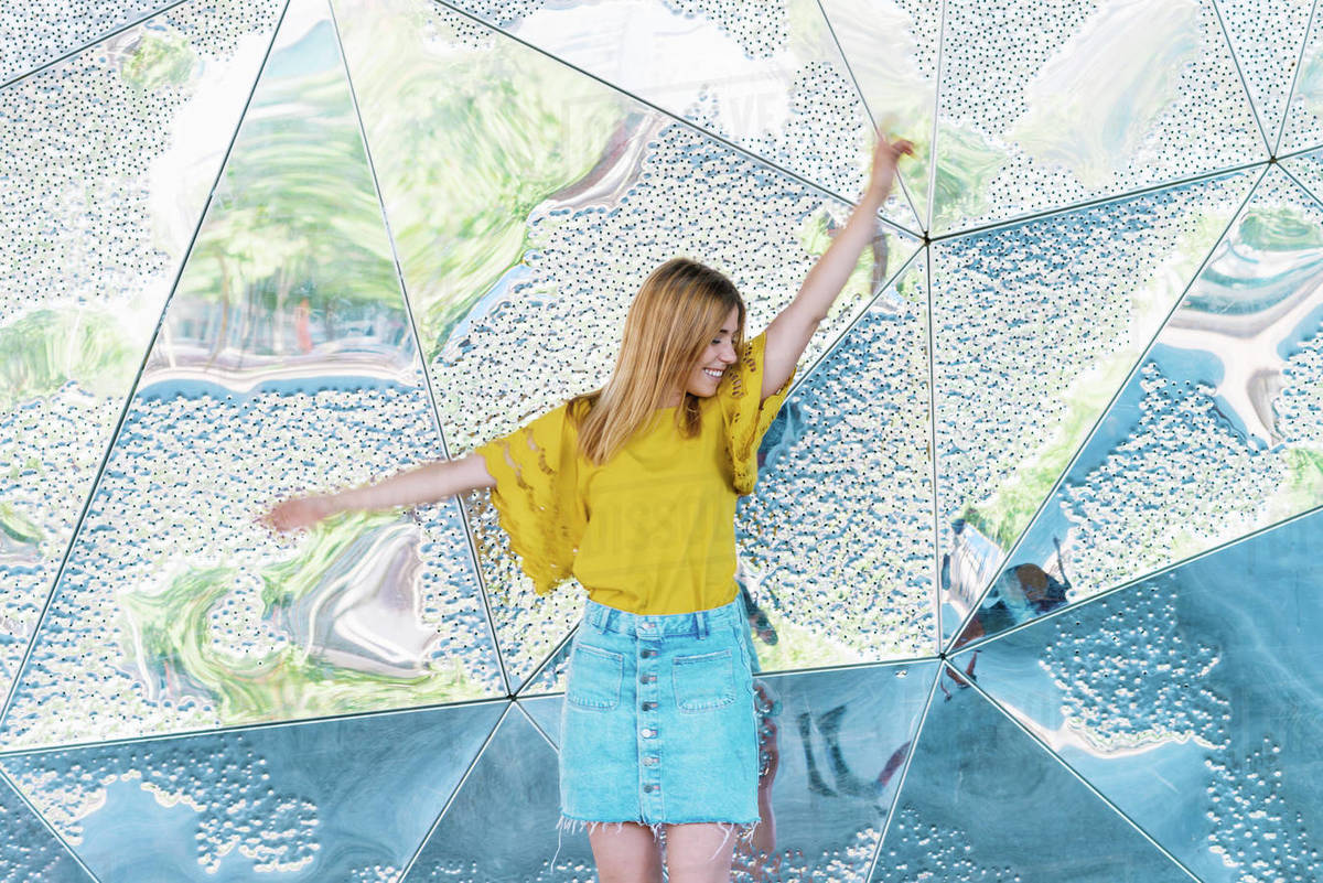 Young stylish cheerful female model posing with hand in air on metal ...