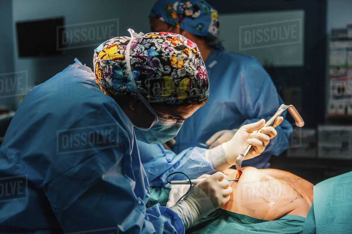 Side view of doctor in surgical gown and protective mask cutting breast ...