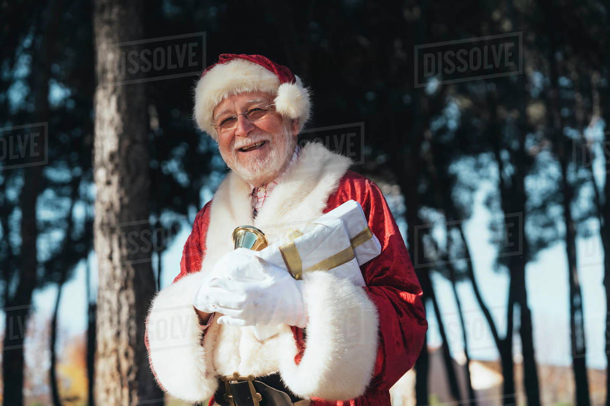 Cheerful senior man in costume of Santa Claus standing with present and ...