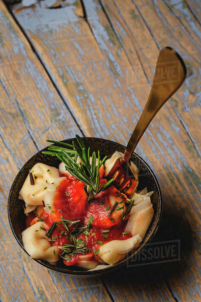 Cooked ravioli with tomato sauce and herbs in bowl next to fork and ...
