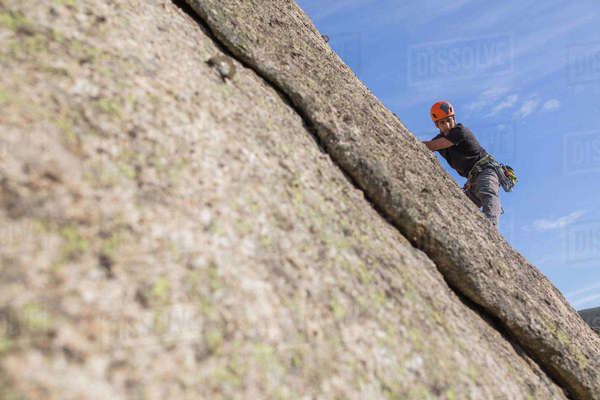 From below man climbing a rock in nature with climbing equipment ...