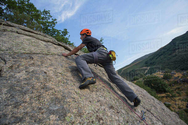 From below man climbing a rock in nature with climbing equipment ...