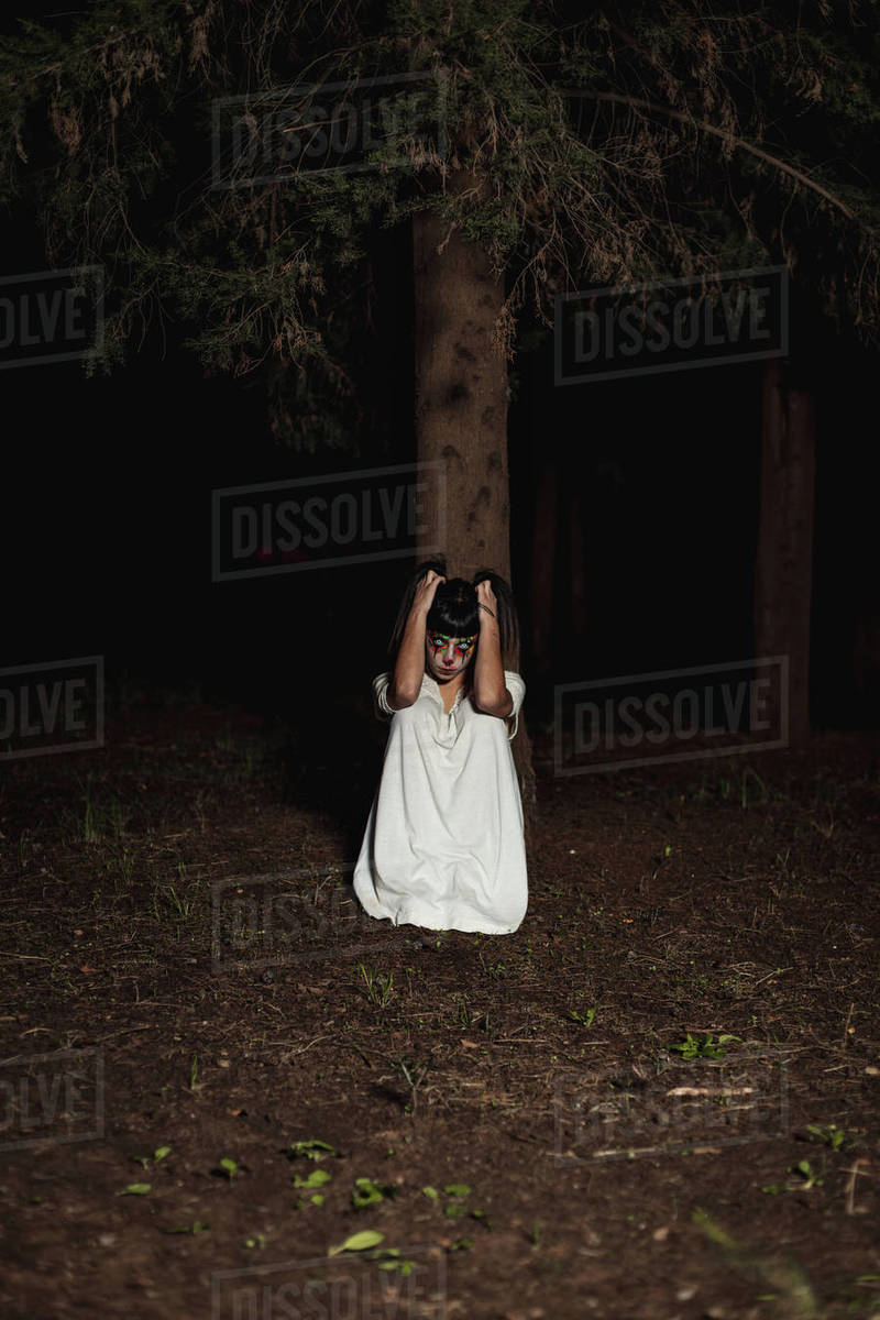 Spooky female sitting on ground in woods at night and touching hair ...