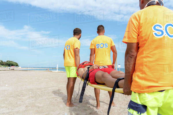Back view of crop anonymous lifeguards in uniform carrying stretcher ...