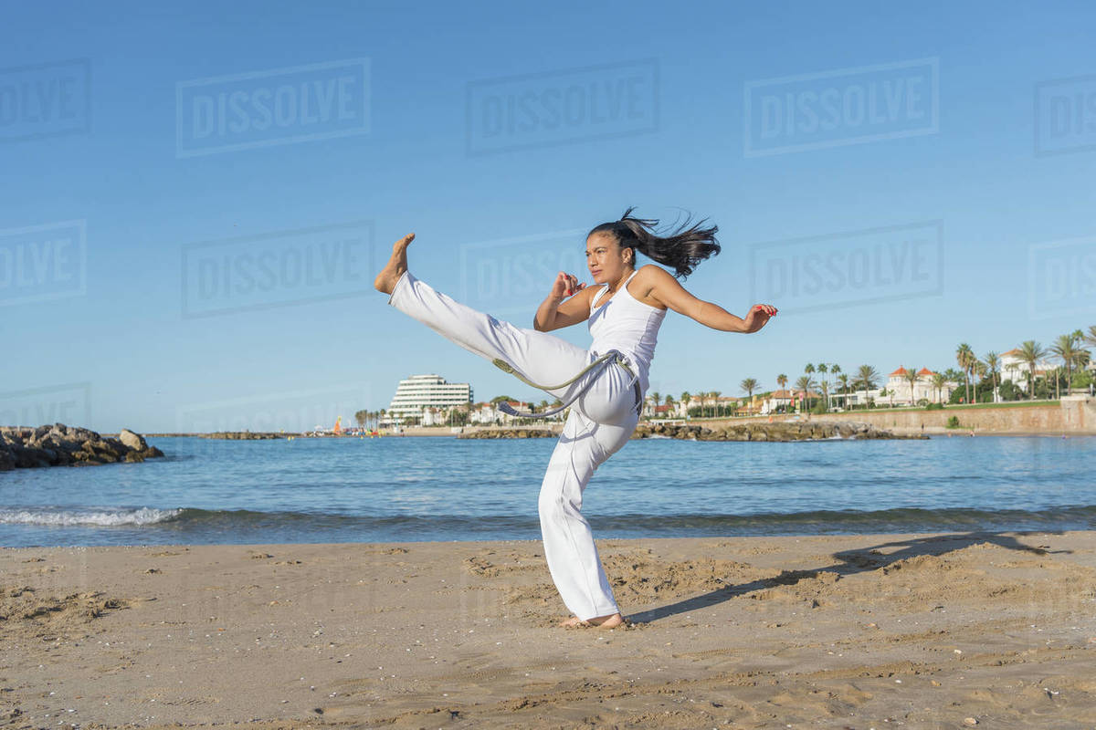 Young focused ethnic female in capoeira clothes showing balance trick ...
