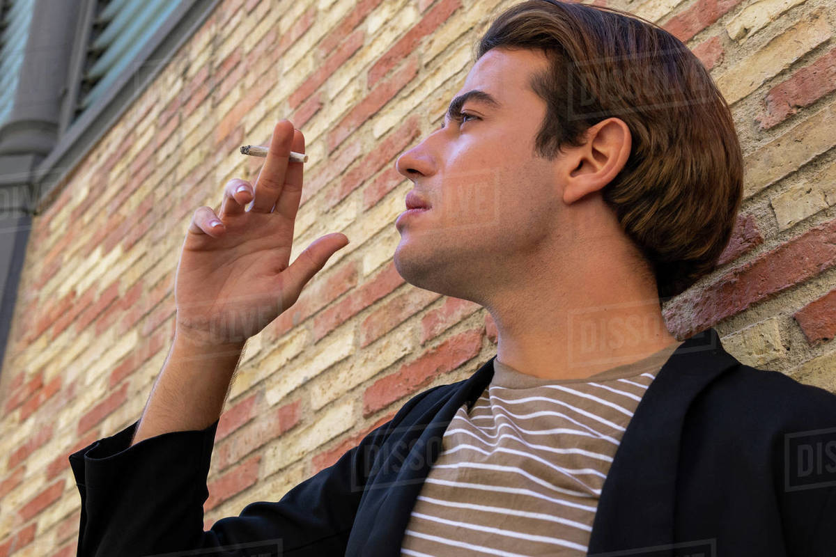 Side view of crop young trendy concentrated male smoking cigarette on ...