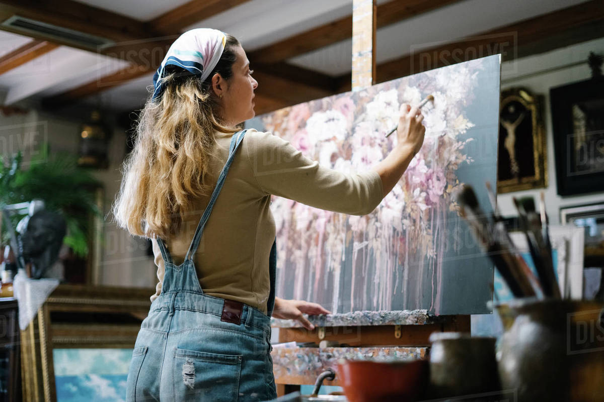 Back view of female artist standing near easel and drawing colorful ...