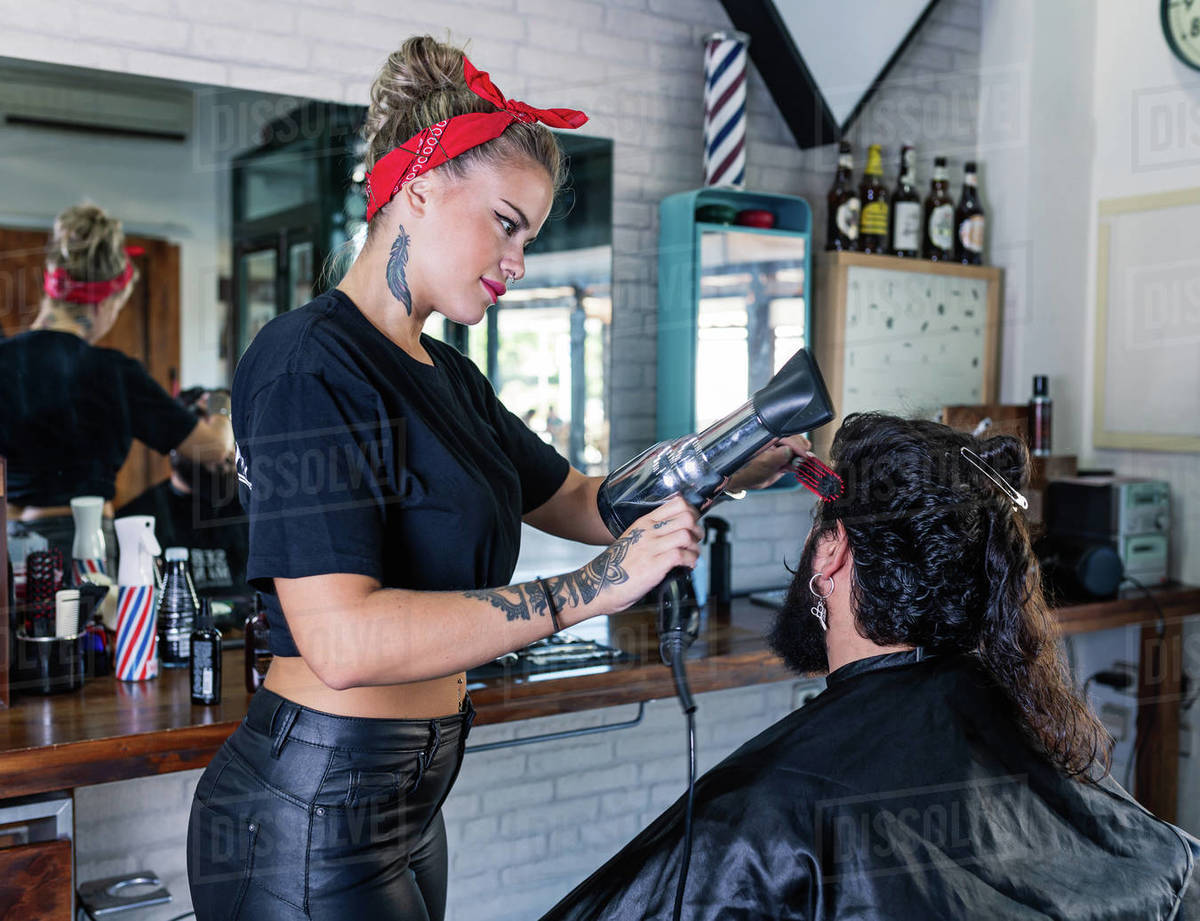 Side view of stylish female master in black leather pants drying hair ...