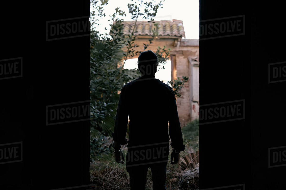 Back view of black silhouette of man standing in front of dark doorway ...