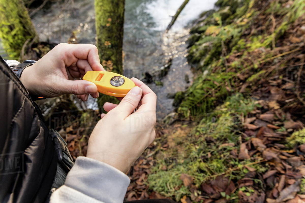 Crop hands of faceless tourist using compass while hiking near small ...