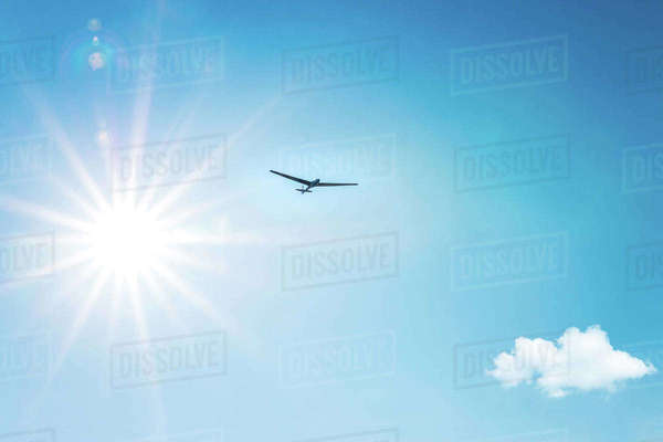 From below aircraft flying in blue sky near small cloud and vivid sun ...