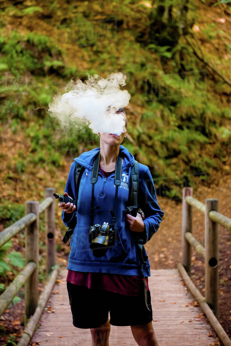 Faceless woman with camera standing on wooden bridge behind thick smoke ...