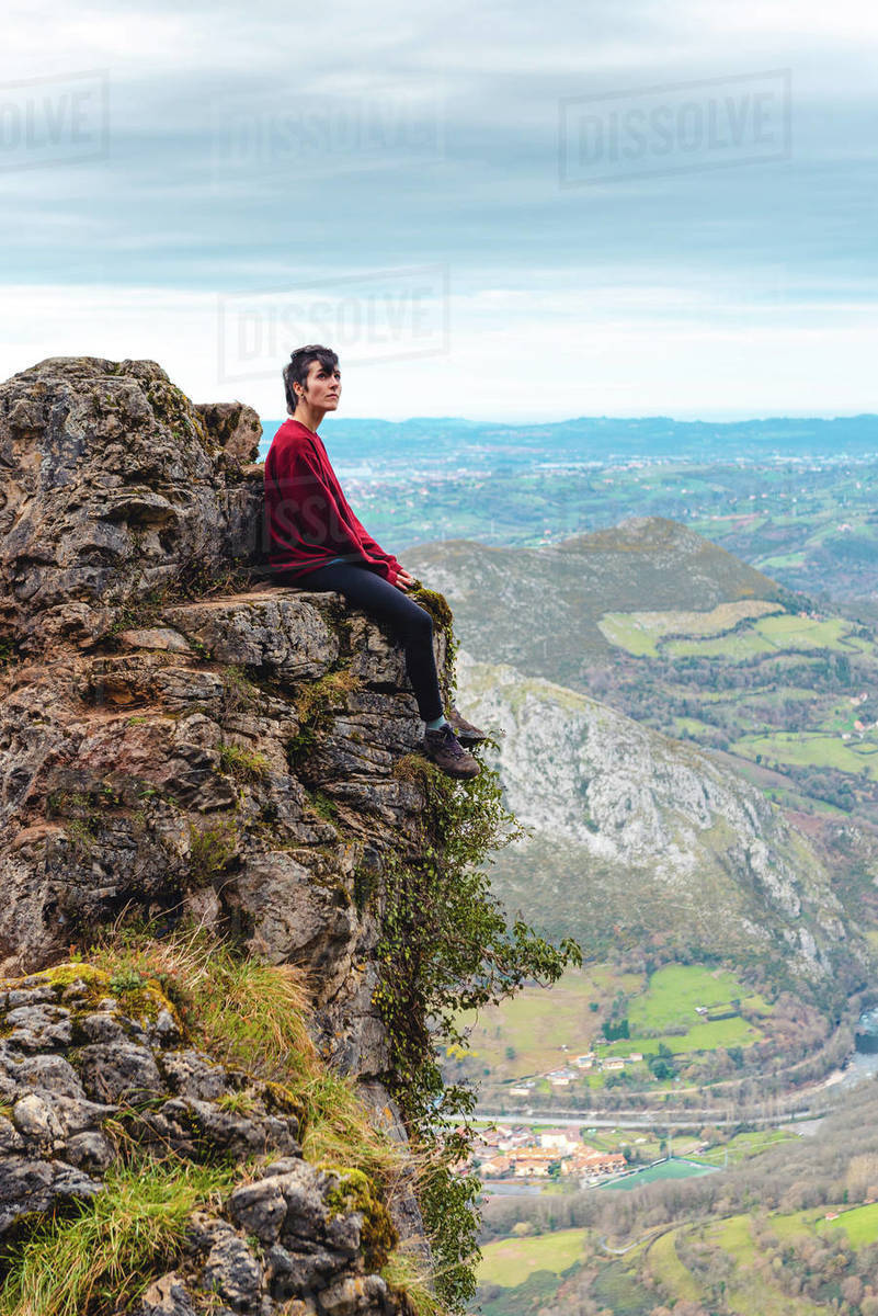 Side view of tourist sitting on edge of cliff enjoying freedom and ...