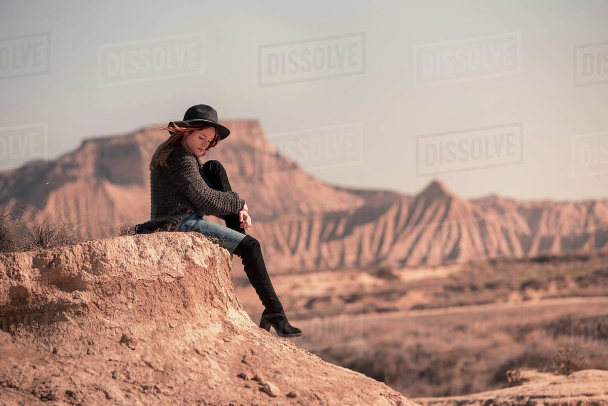 Side view of young woman in trendy outfit embracing knee and sitting on ...