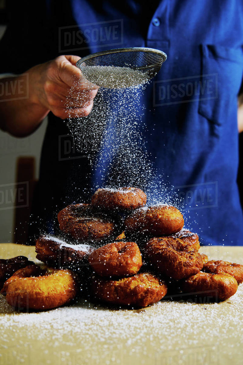 Unrecognizable person using sieve to spill powdered sugar on stack of ...