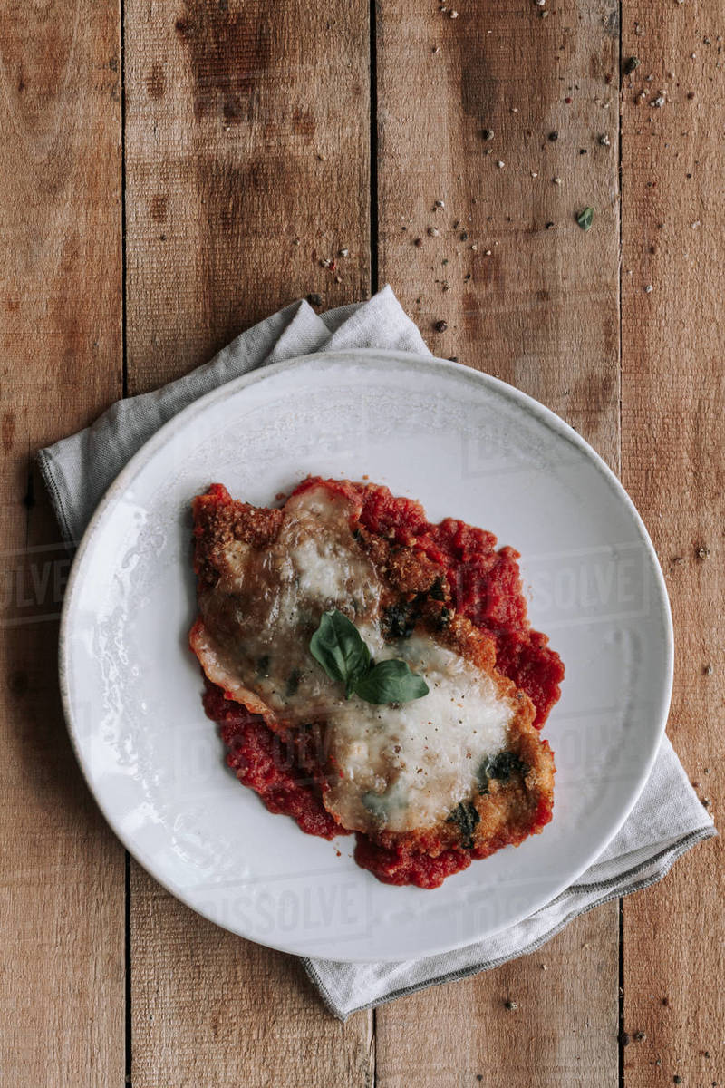 Top view of piece of roasted chicken with Parmesan and leaf of basil ...