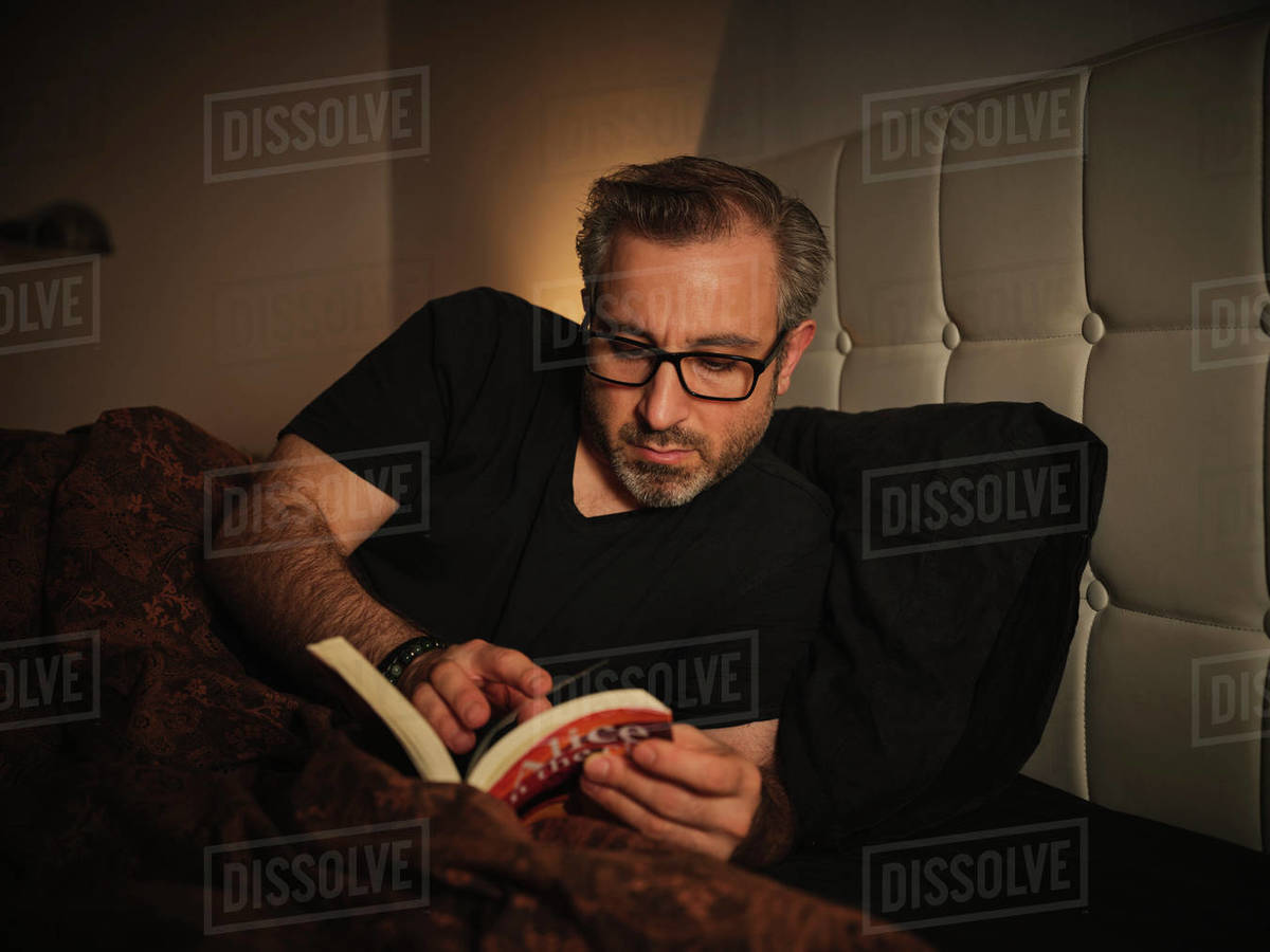 Relaxed man in bed reading a book before sleeping and resting - Stock ...