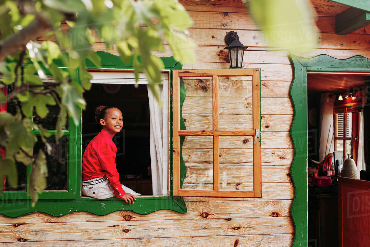 Cheerful black child in red shirt and white pants looking through open ...