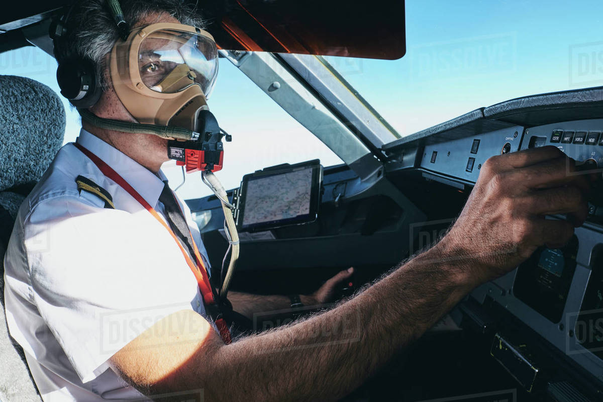 Side view of professional male aviator in oxygen mask turning switch on ...